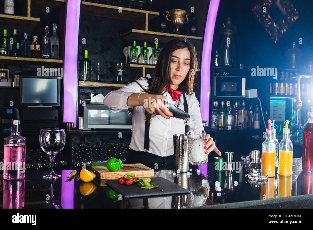 Female barkeeper in stylish outfit adding ice cubes into a glass while ...
