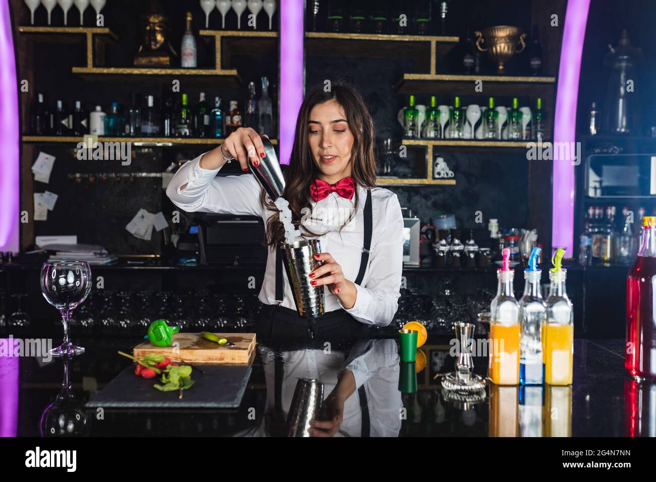 Female barkeeper in stylish outfit adding ice cubes into shaker while ...