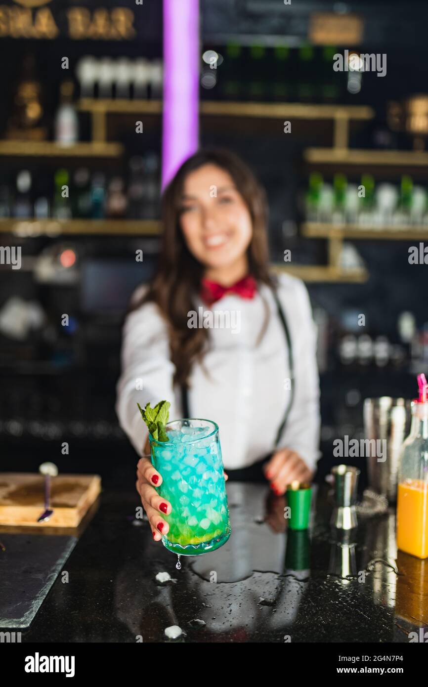 Blurred unrecognizable female barkeeper in stylish outfit serving blue ...