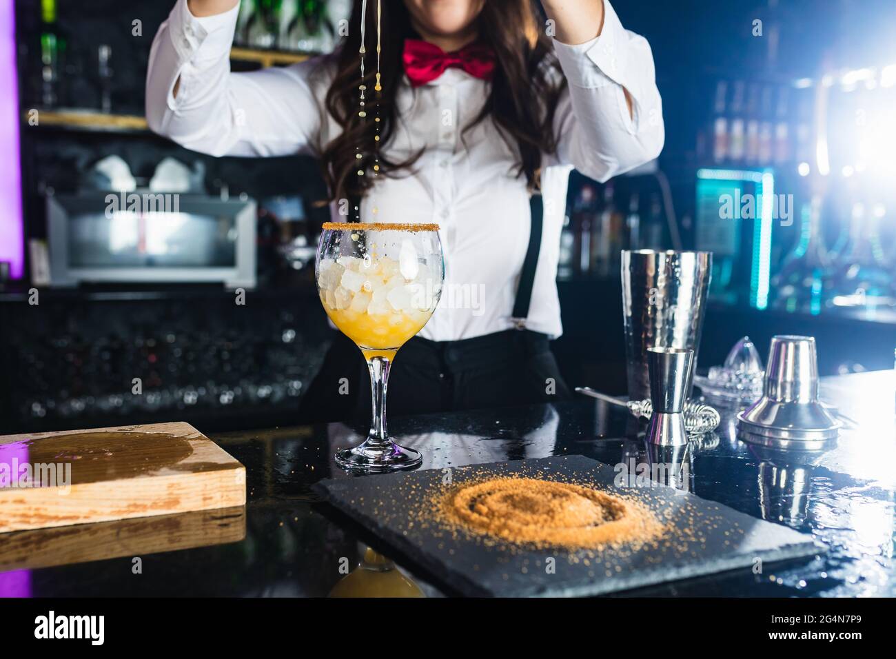 Cropped unrecognizable female barkeeper in stylish outfit adding yellow ...