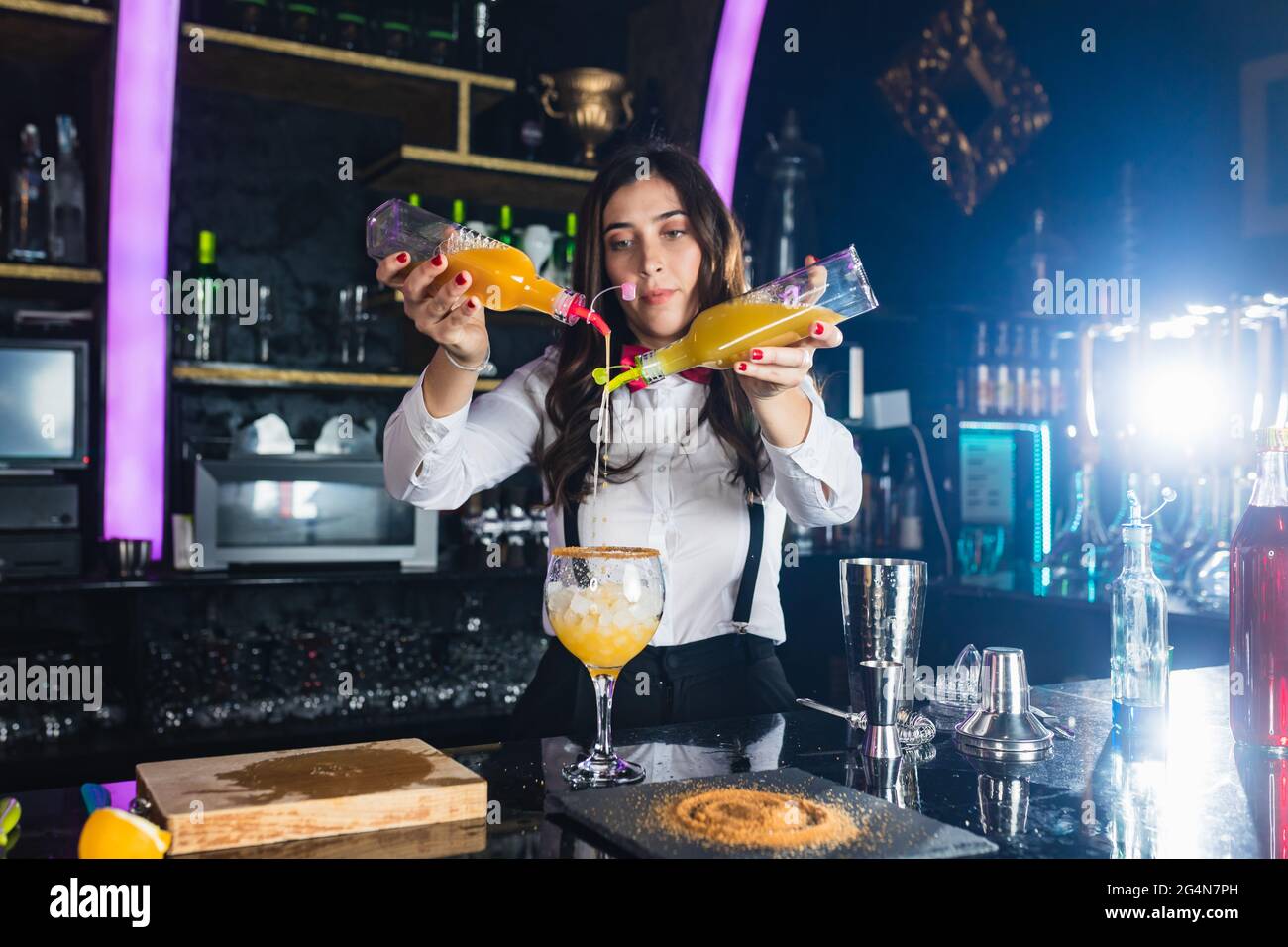 Focused female barkeeper in stylish outfit adding yellow colorant ...