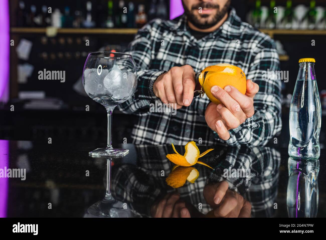 Cropped unrecognizable male barkeeper adding orange peel into a glass ...