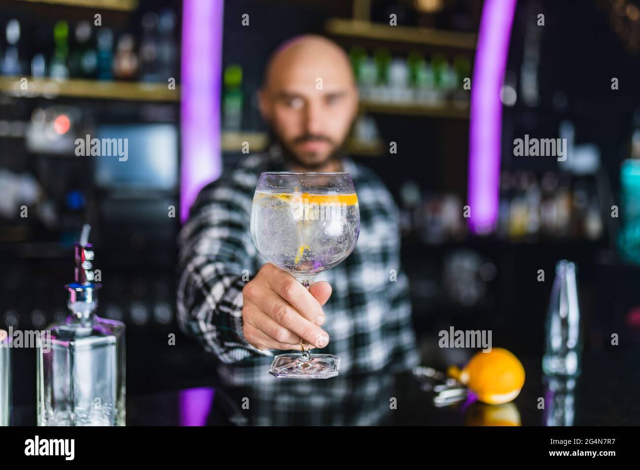Blurred unrecognizable male barkeeper serving cocktail with orange peel ...