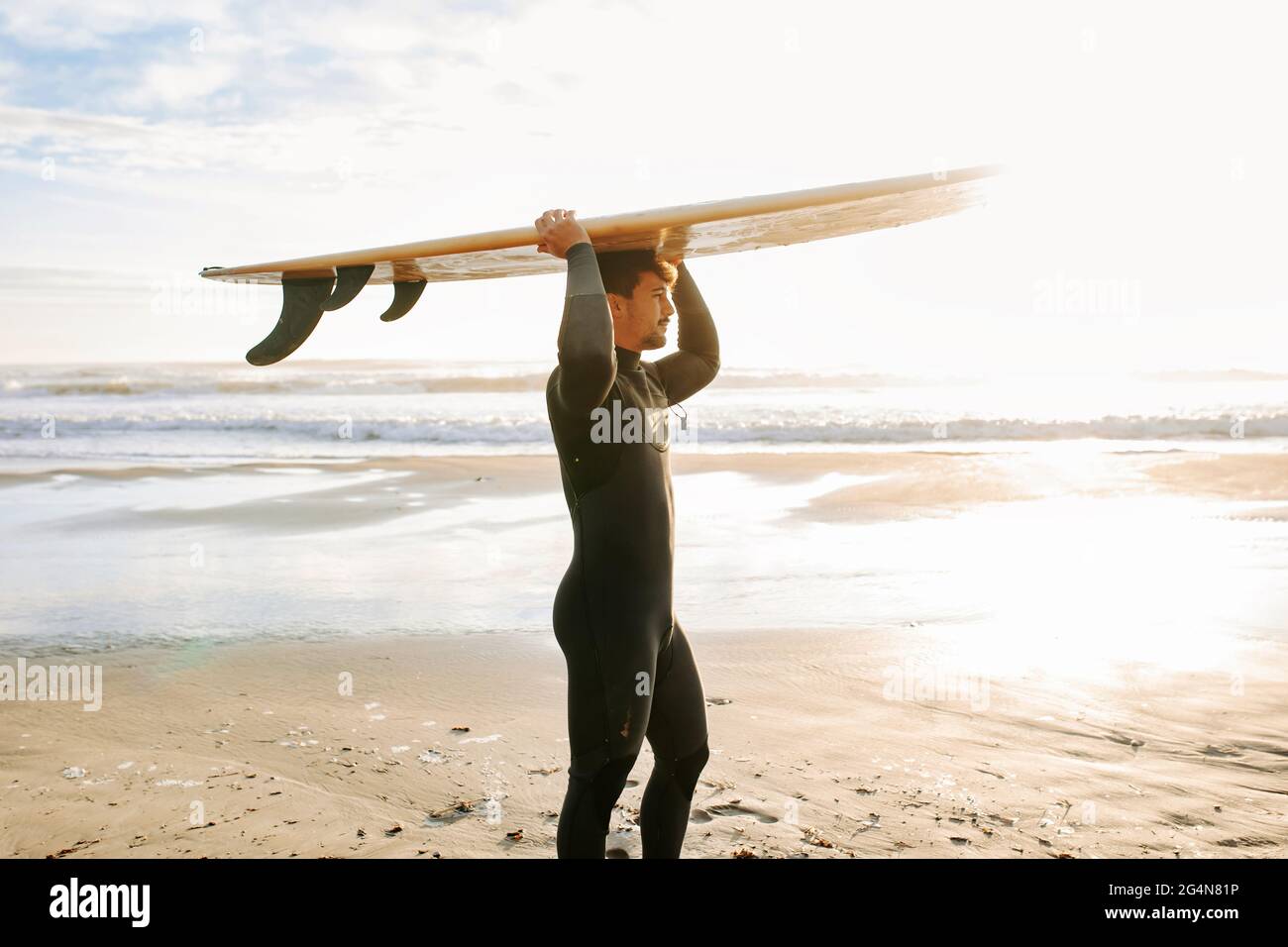 Side view of surfer man dressed in wetsuit walking on the beach with ...