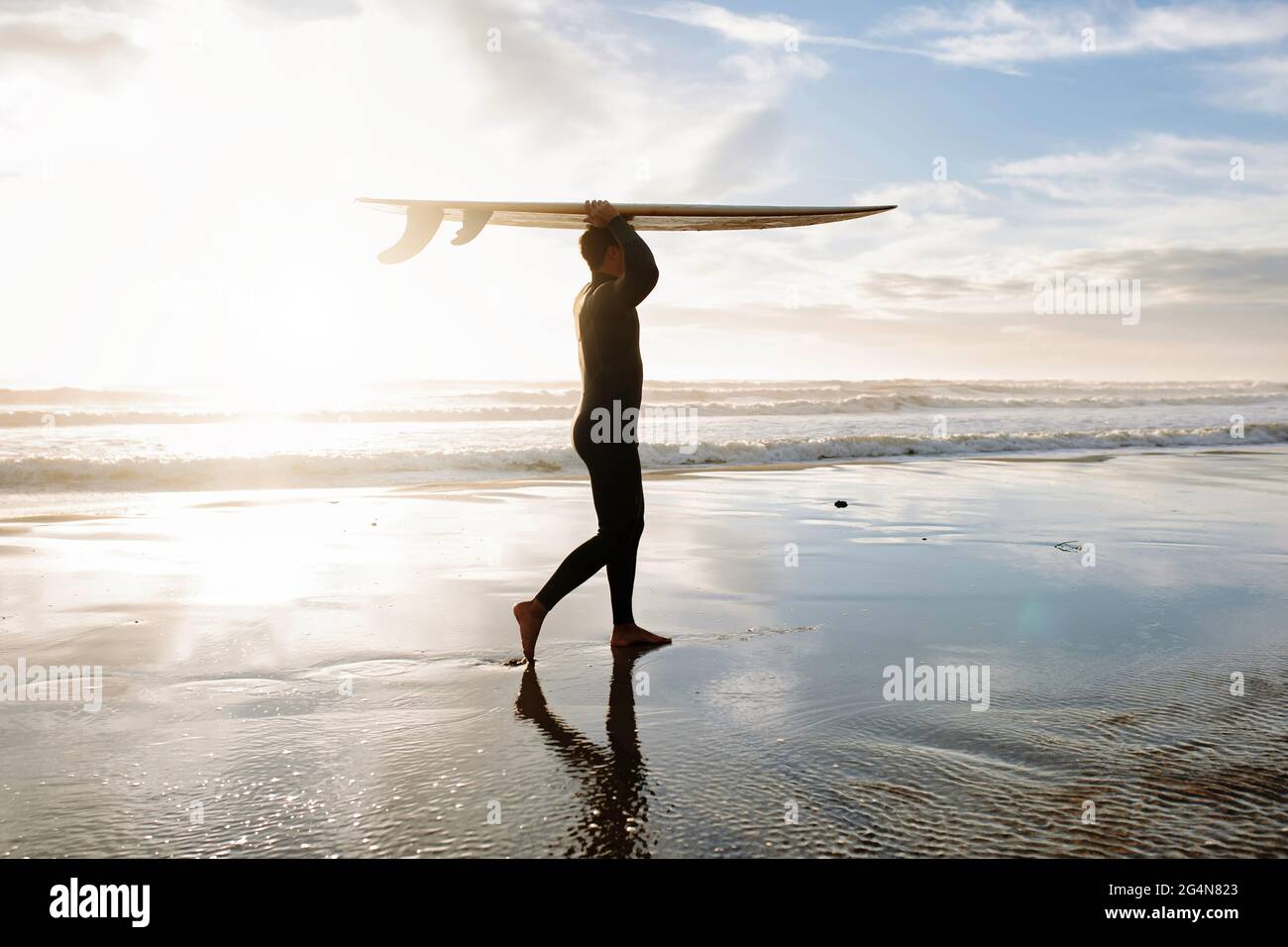 Side view of surfer man dressed in wetsuit walking on the beach with ...