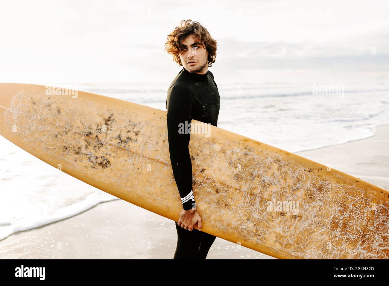 Side view of surfer man dressed in wetsuit standing looking away with ...