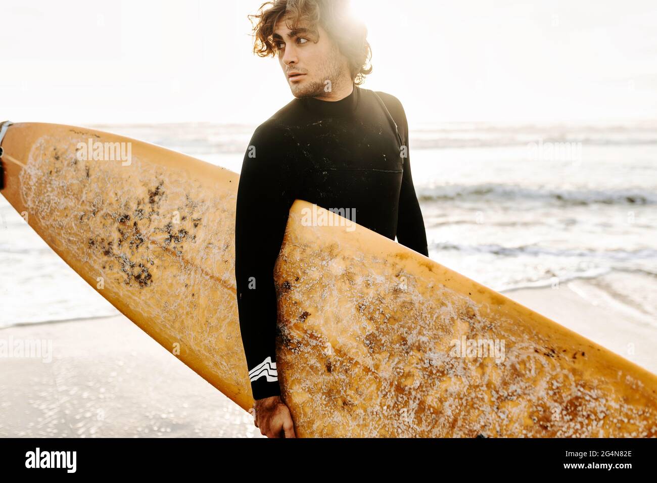 Side view of surfer man dressed in wetsuit standing looking away with ...