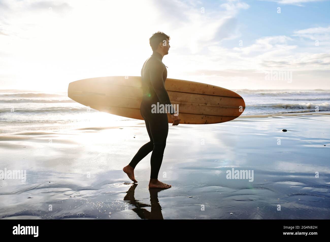 Side view of surfer man dressed in wetsuit walking on the beach with ...