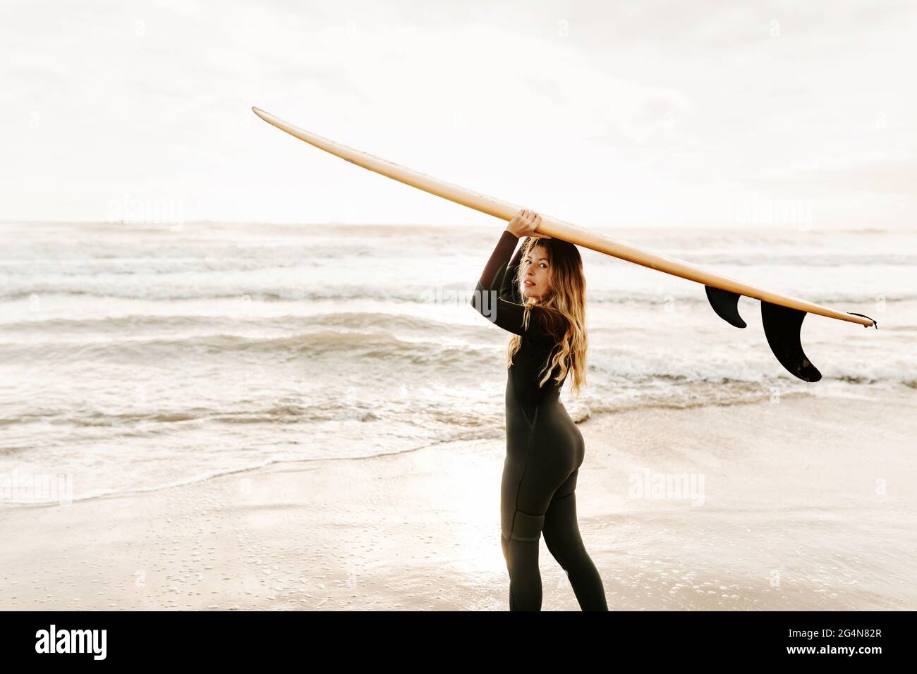 Side view of female surfer dressed in wetsuit standing looking at ...