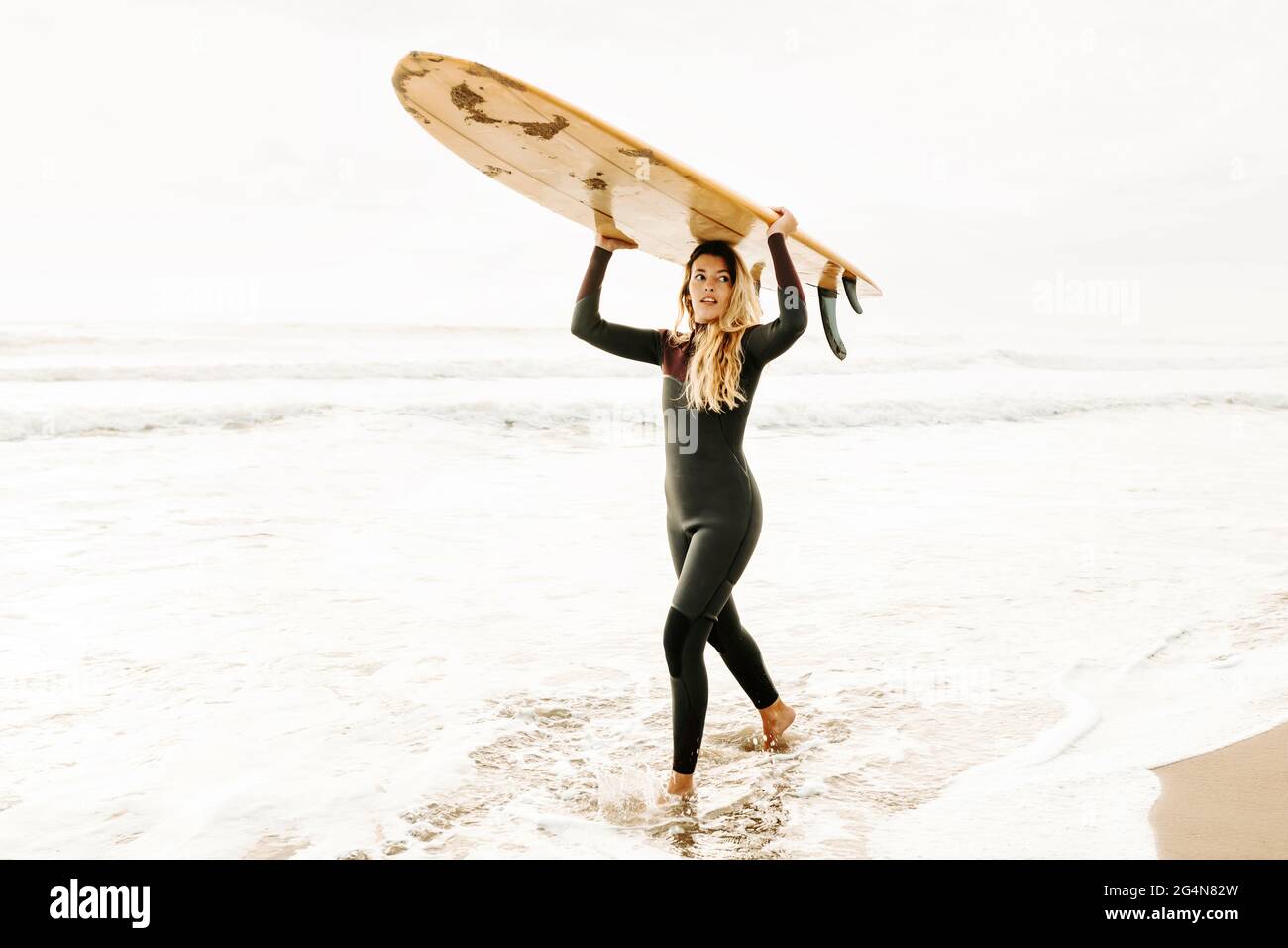 Side view of female surfer dressed in wetsuit walking looking away ...