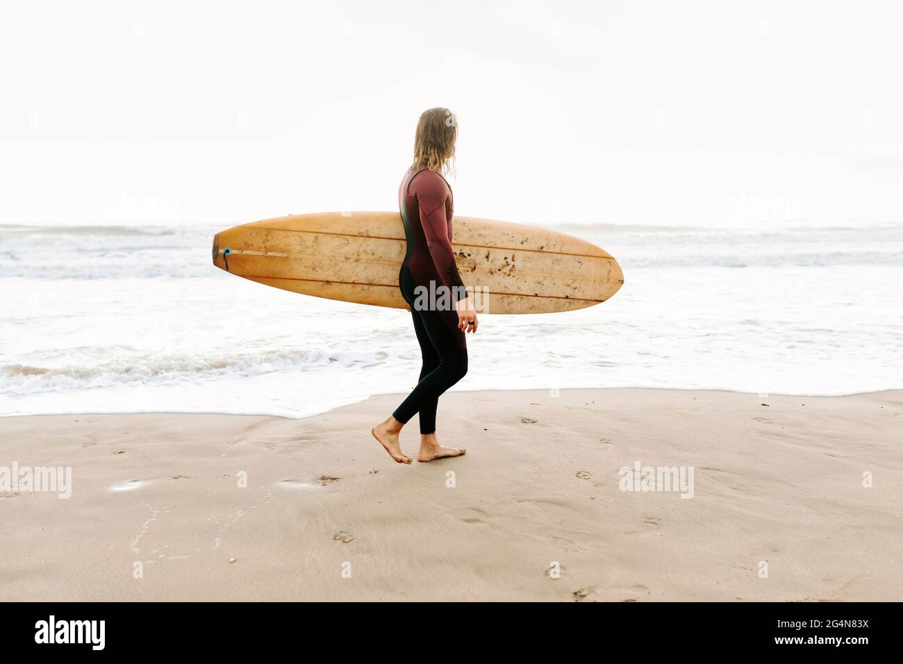 Side view of surfer man dressed in wetsuit walking looking away with ...