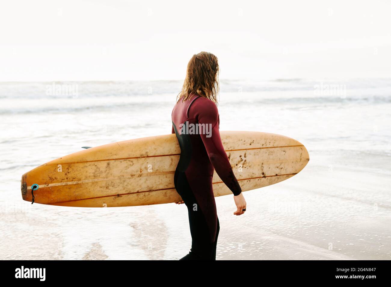 Side view of surfer man dressed in wetsuit walking looking away with ...