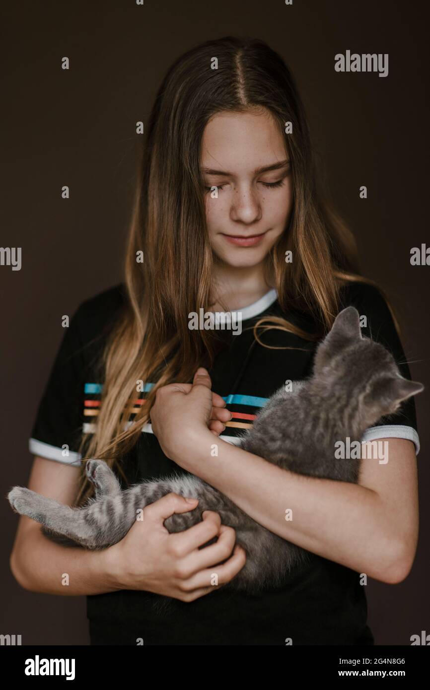Dreamy teenage girl holding fluffy cute cat on brown background in ...