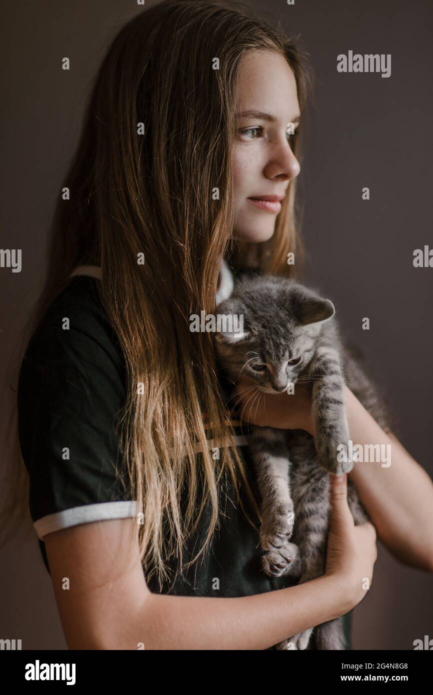 Dreamy thoughtful teenage girl holding fluffy cute cat on brown ...