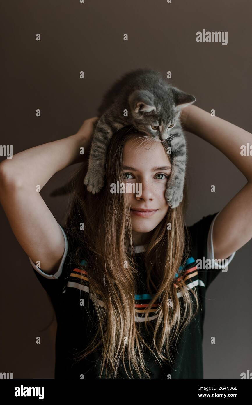 Dreamy teenage girl with fluffy cute cat on head on brown background in ...