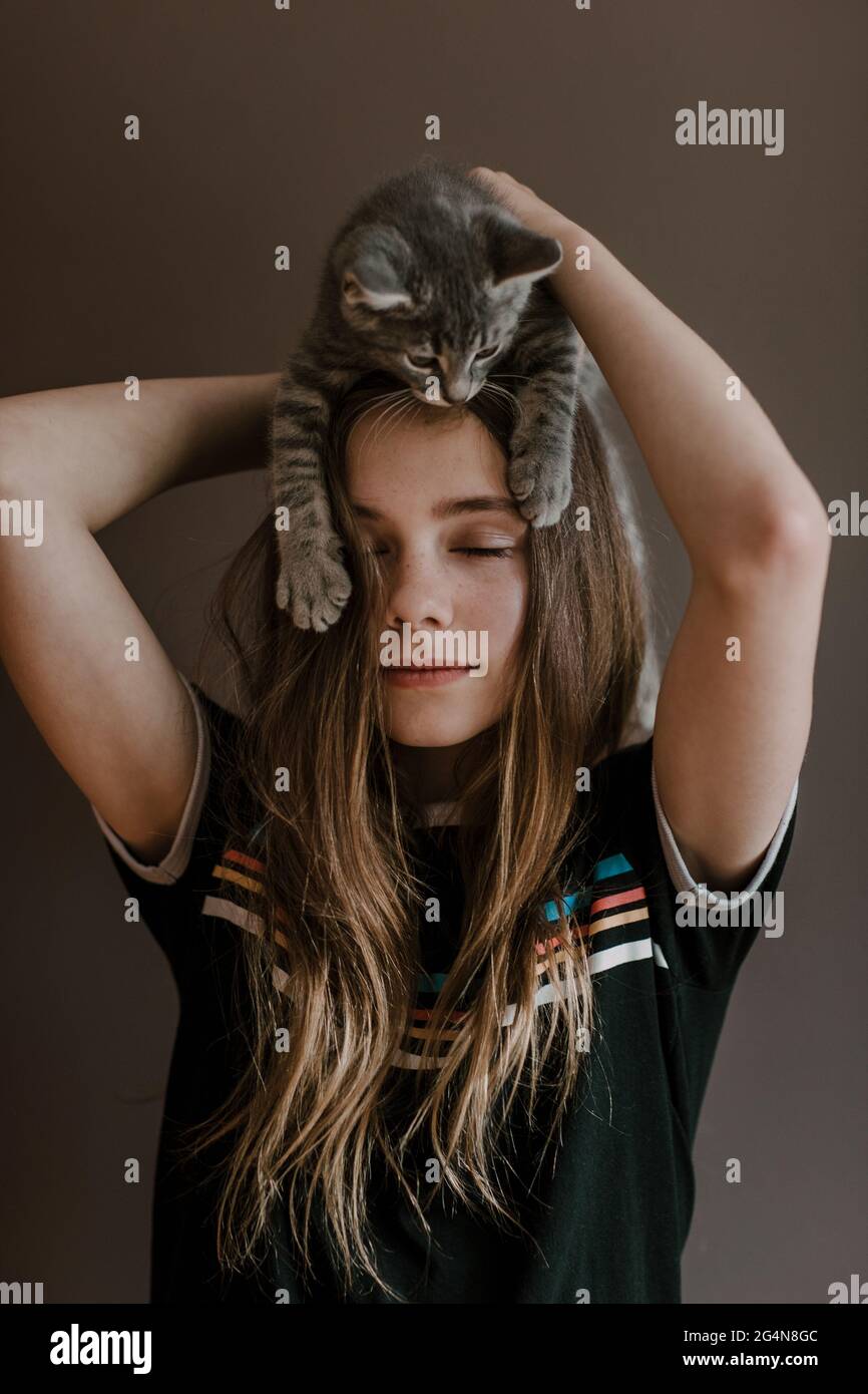 Dreamy teenage girl with fluffy cute cat on head on brown background in ...