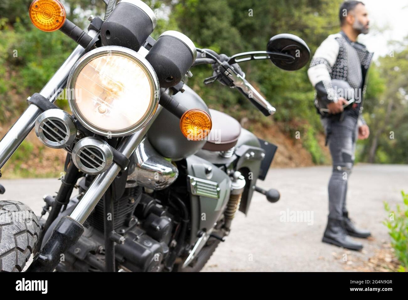 Serious male biker in jeans and leather jacket holding helmet in hand ...