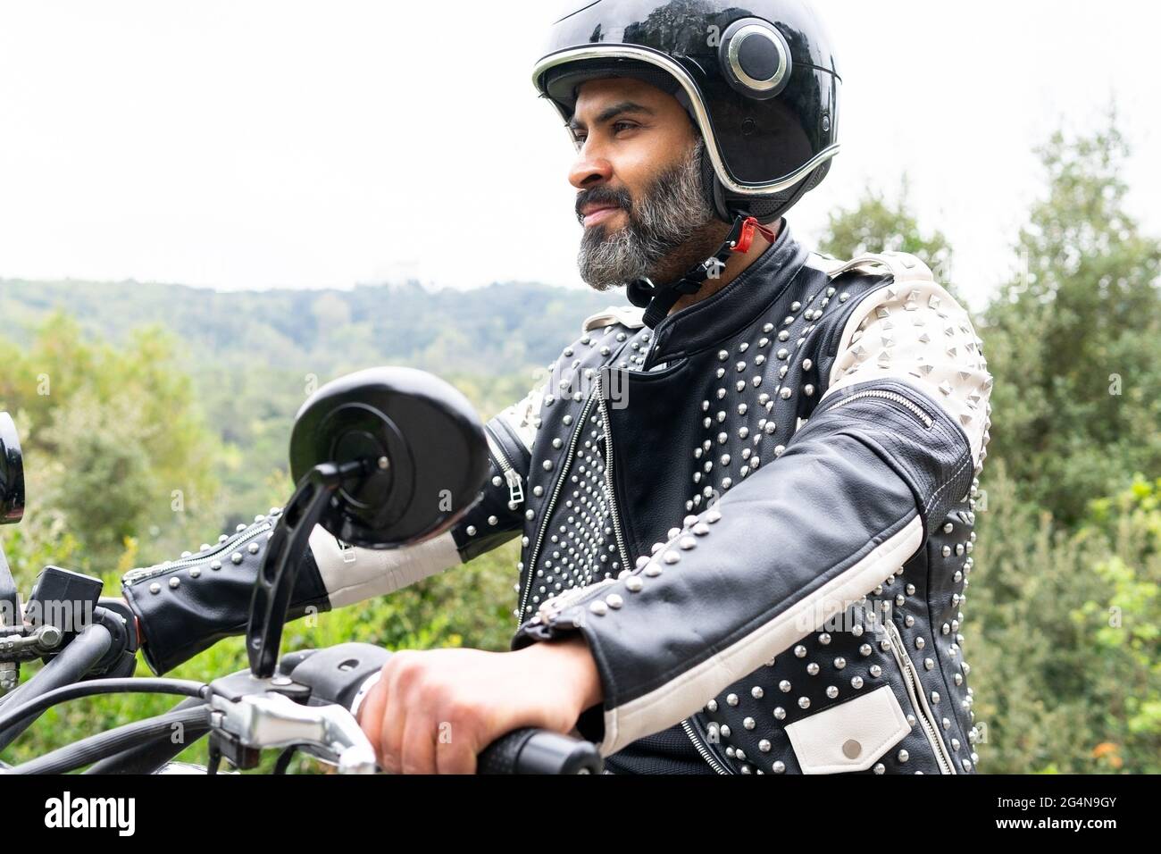 Bearded ethnic male biker in black leather jacket and helmet riding ...