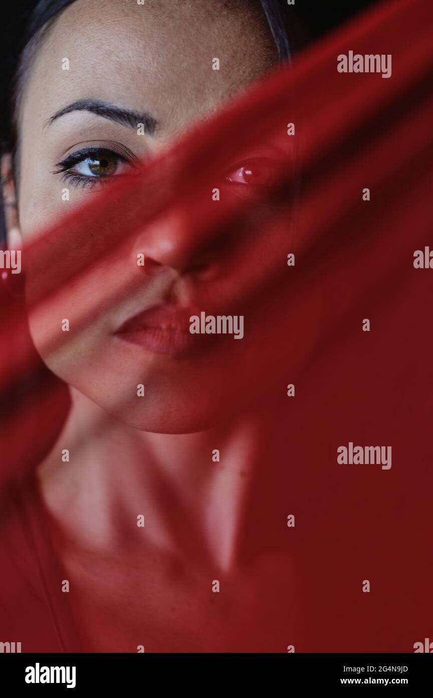 Crop young female with red lips looking at camera behind transparent ...