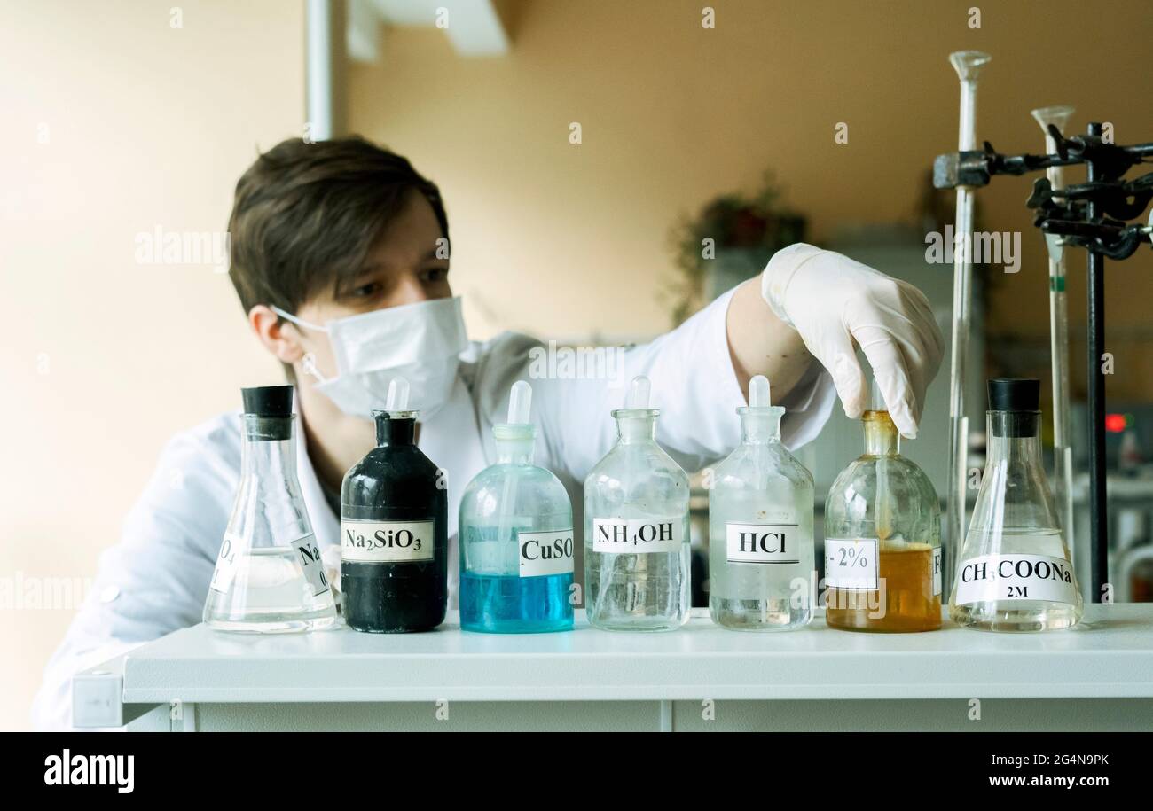 the student in white uniform with glass flasks doing research on the ...