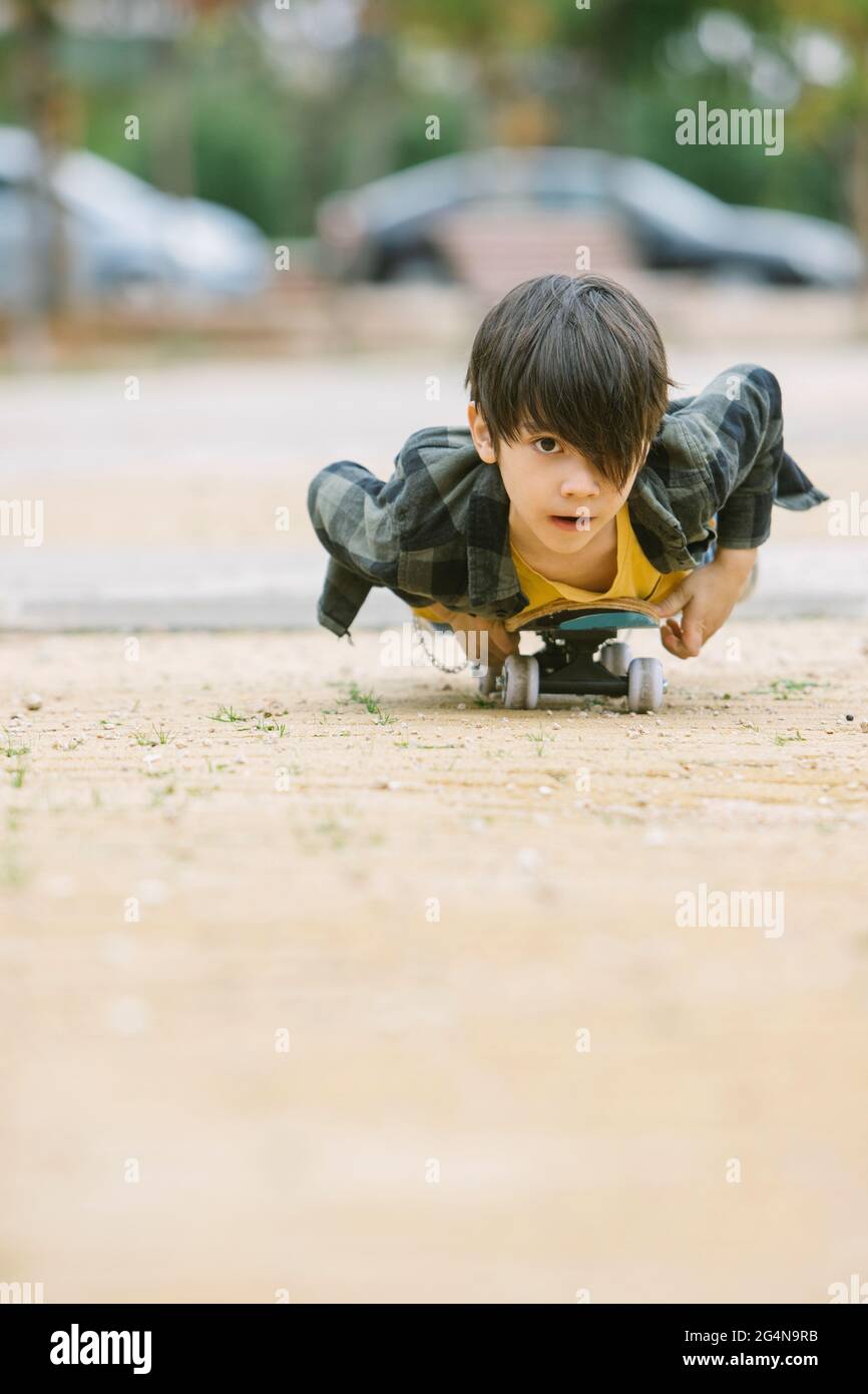 Ground level of skilled boy in casual outfit lying on skateboard while ...