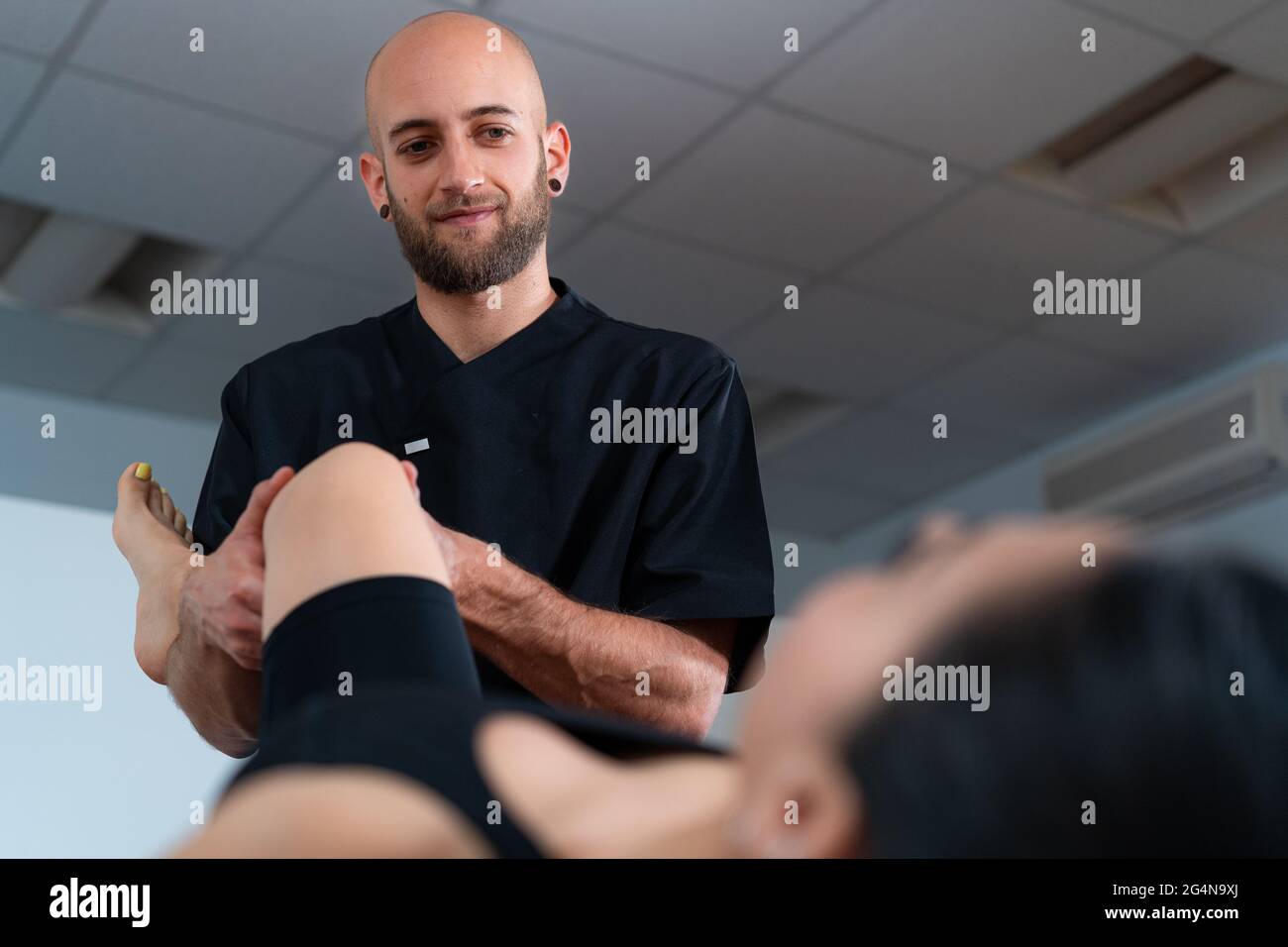 Bald male doctor in black uniform checking up leg of crop ...