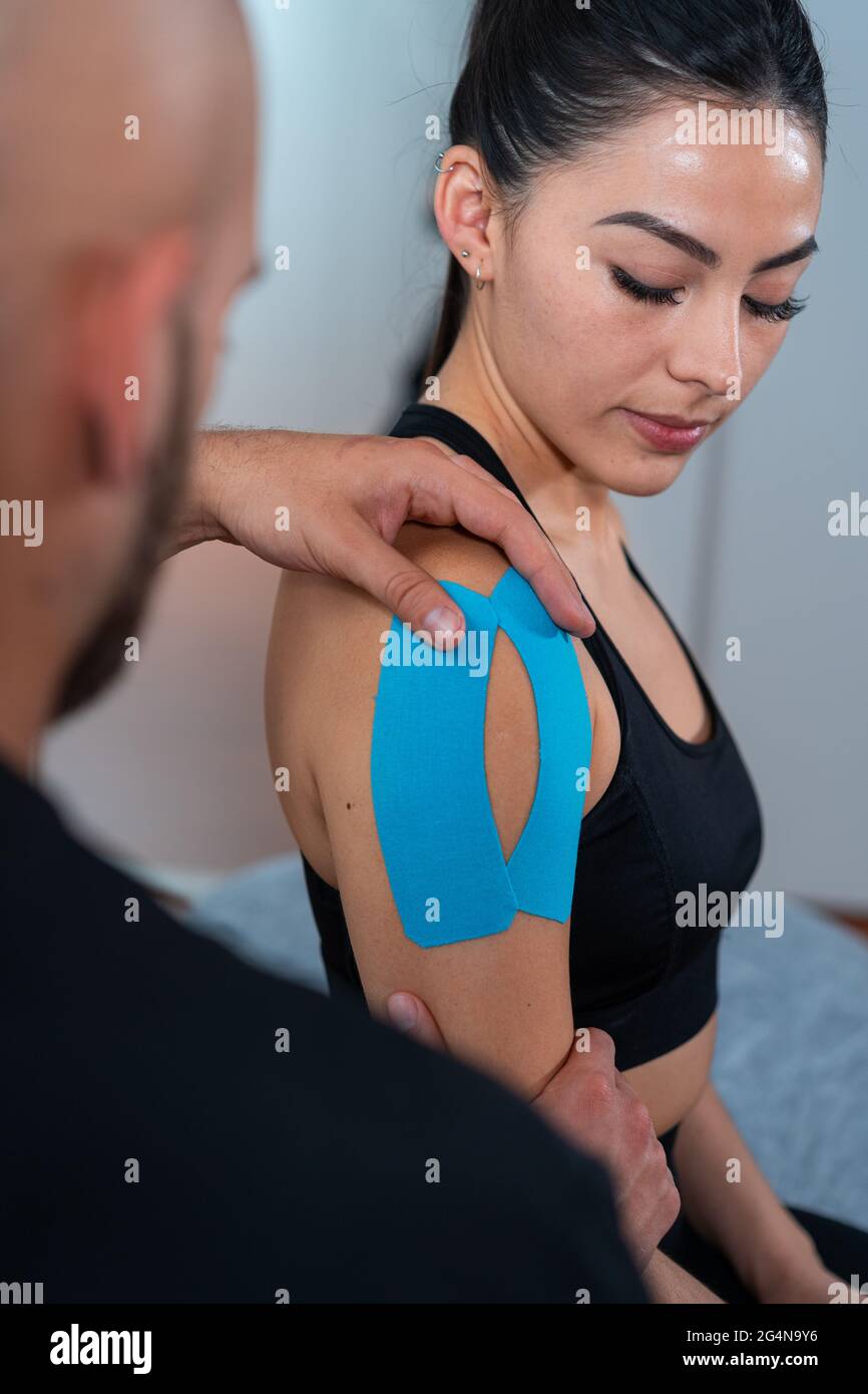 Bearded male physiotherapist applying kinesio tapes on shoulder of female athlete during ...
