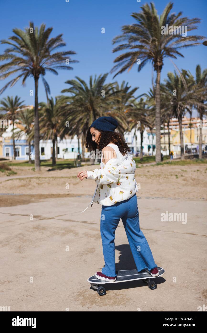 Full body of active female in casual clothes riding skateboard on road ...