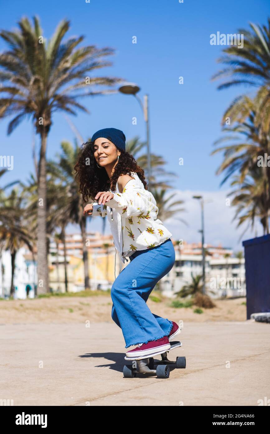 Full body of active happy female in casual clothes riding skateboard on ...
