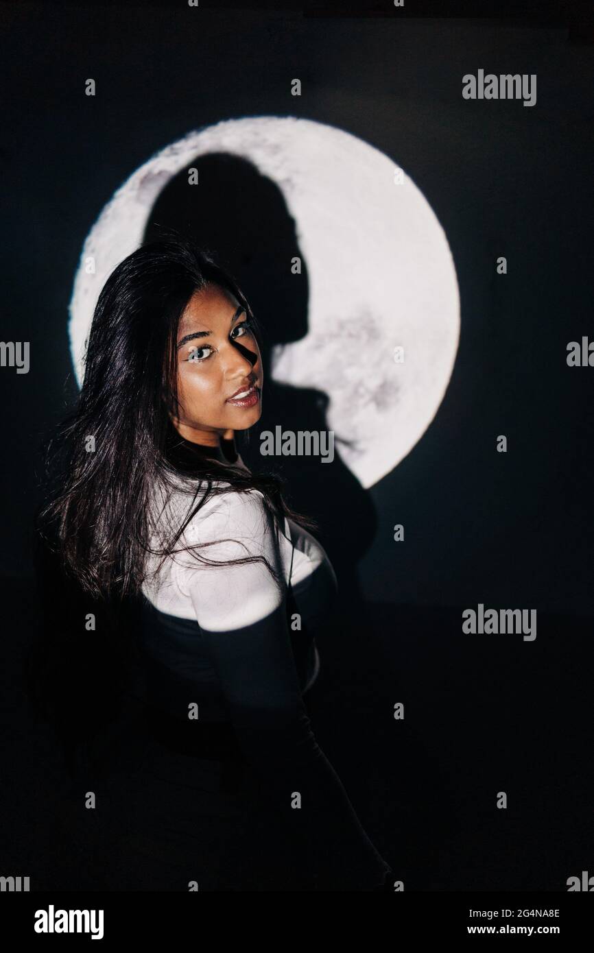 Side view of young Hispanic female looking at camera resting under moon ...