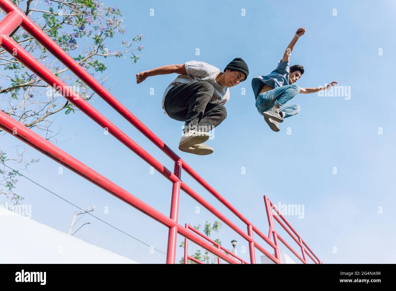 From below fearless male friends jumping above metal railing in city ...