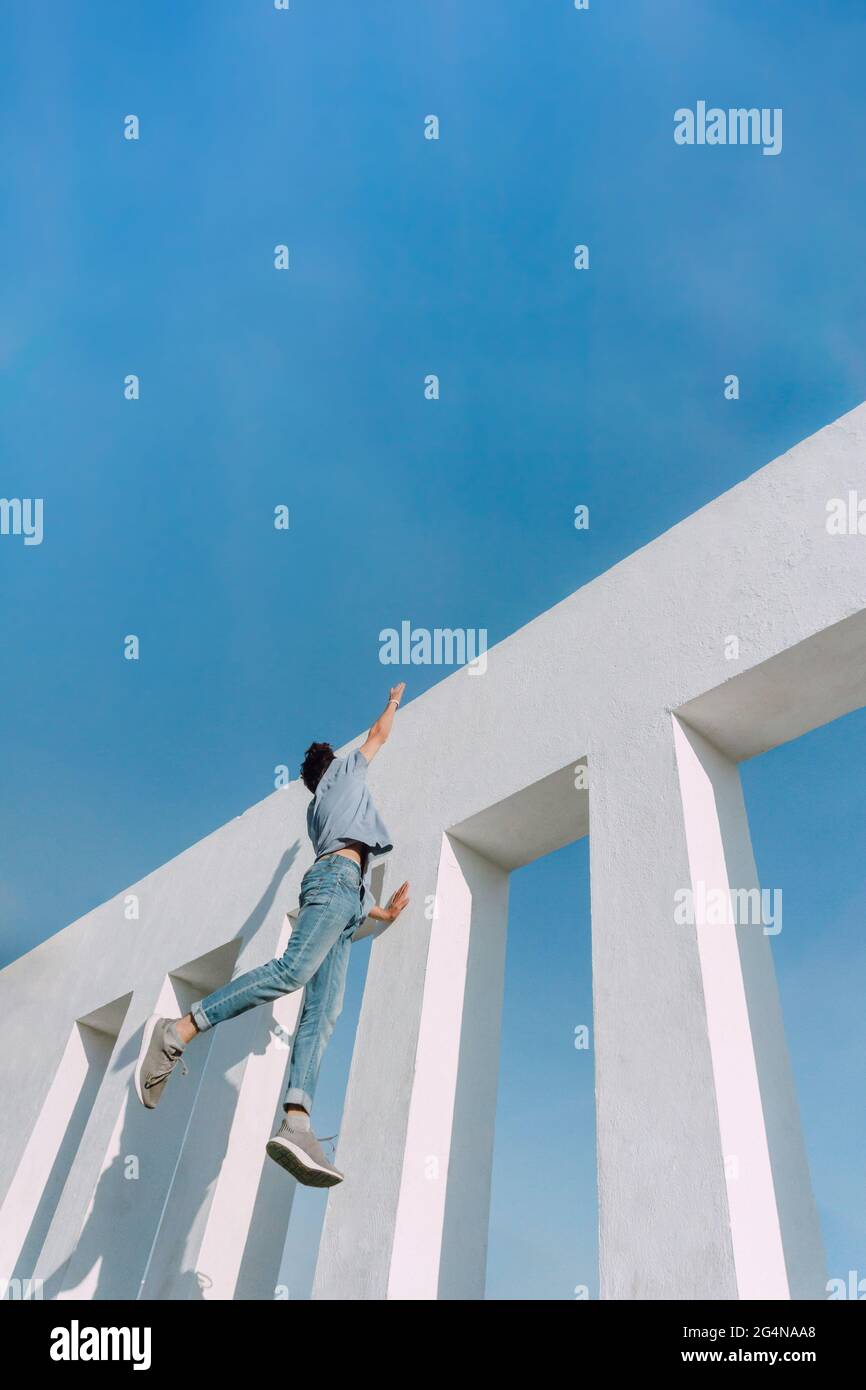 From below of anonymous fearless male hanging on edge of concrete wall ...