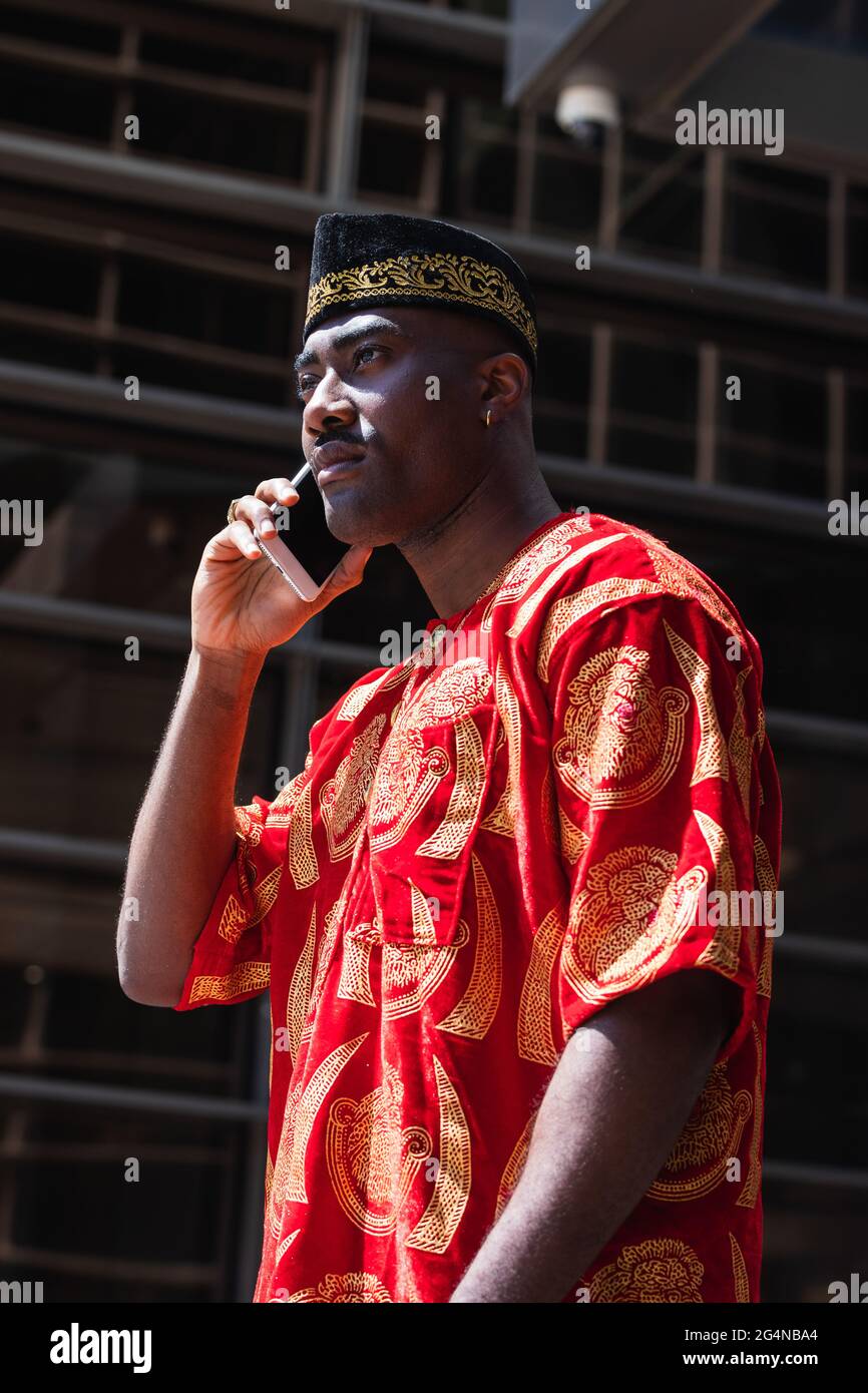 Serious Adult Black Man In Traditional Red Clothes And Kufi Standing Near Building With Glass