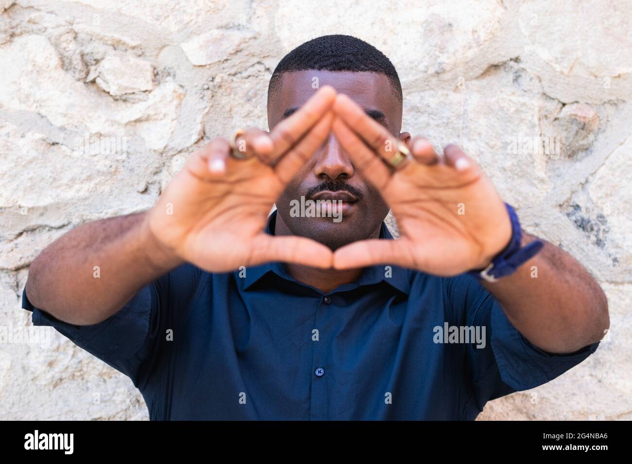 Serious black guy showing triangle shape with hands while covering eyes ...