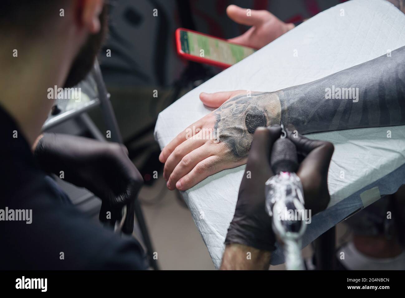 Concentrated male tattooist in gloves making tattoo on hand of client ...