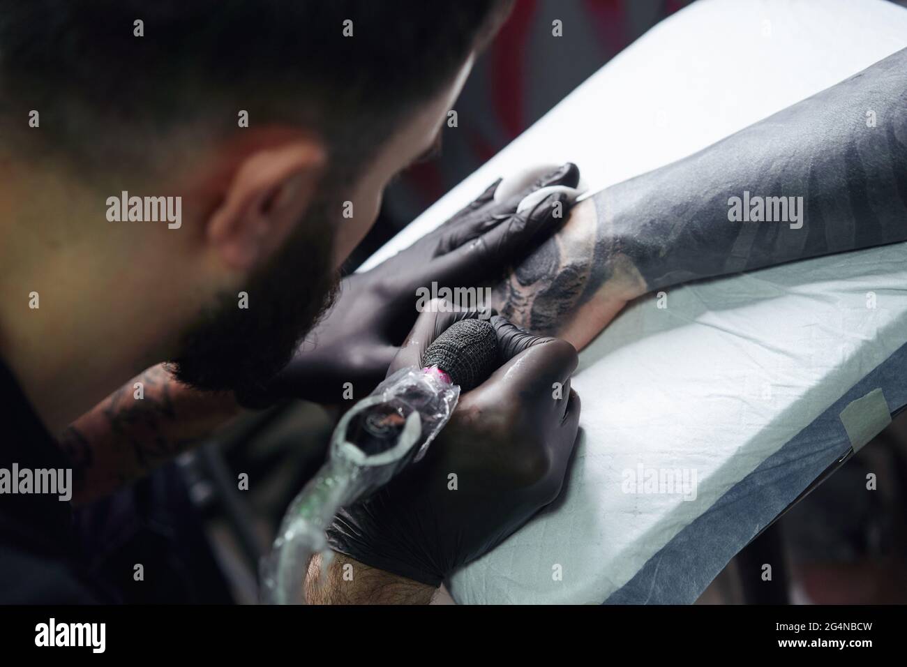 Concentrated male tattooist in gloves making tattoo on hand of client ...