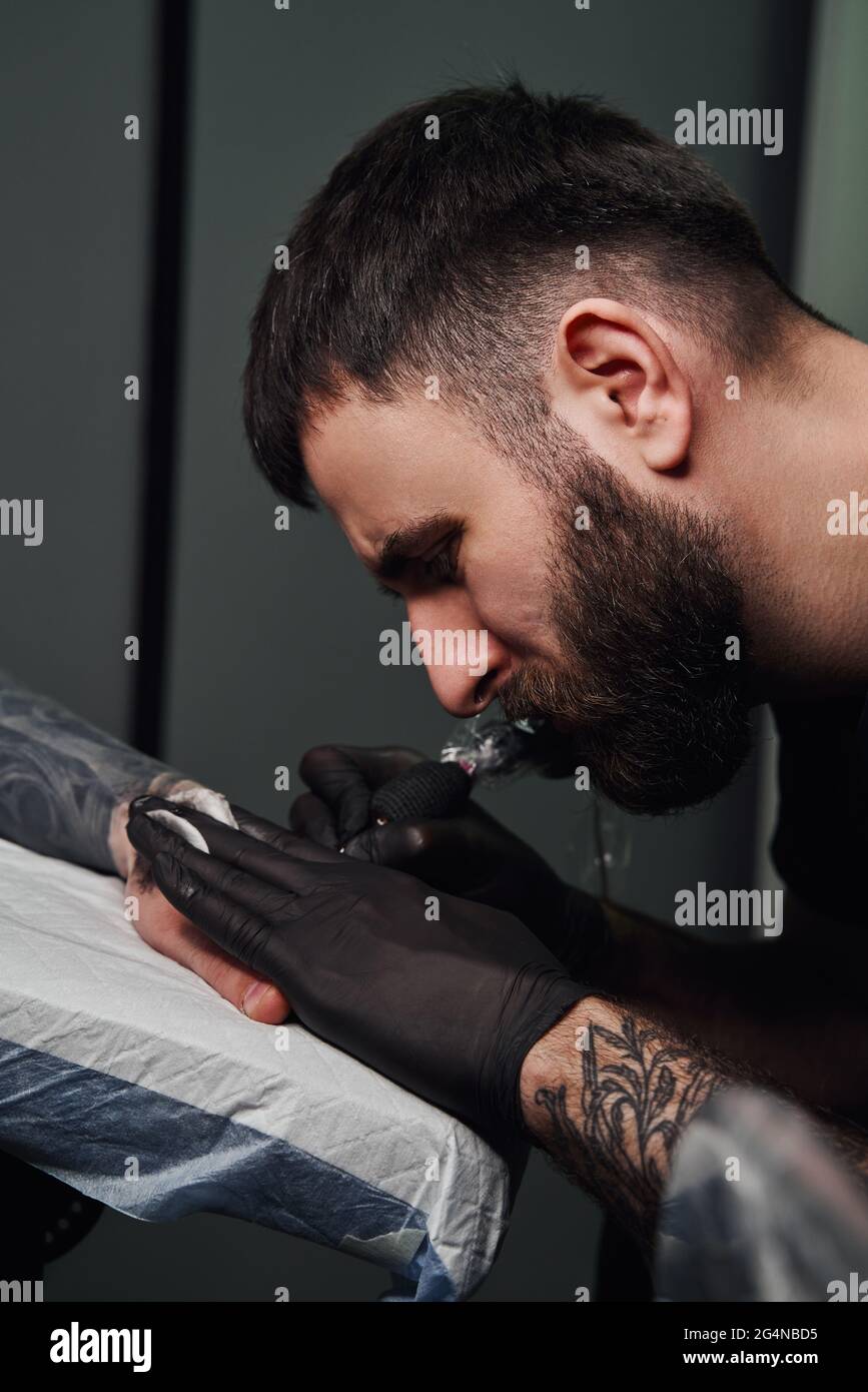 Concentrated male tattooist in gloves making tattoo on hand of client ...