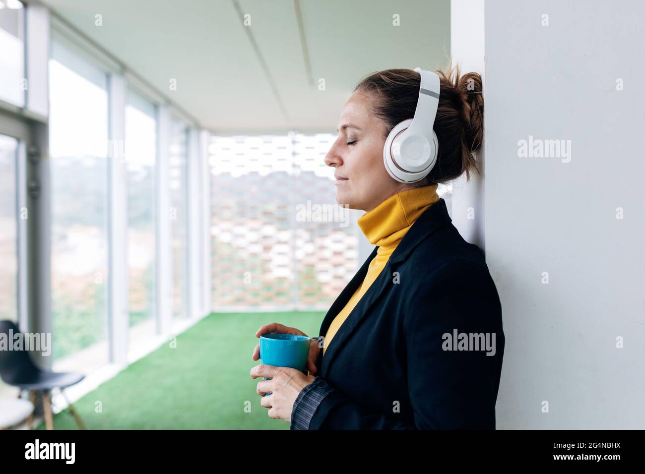 Side view adult female in stylish outfit and headphones with mug with ...