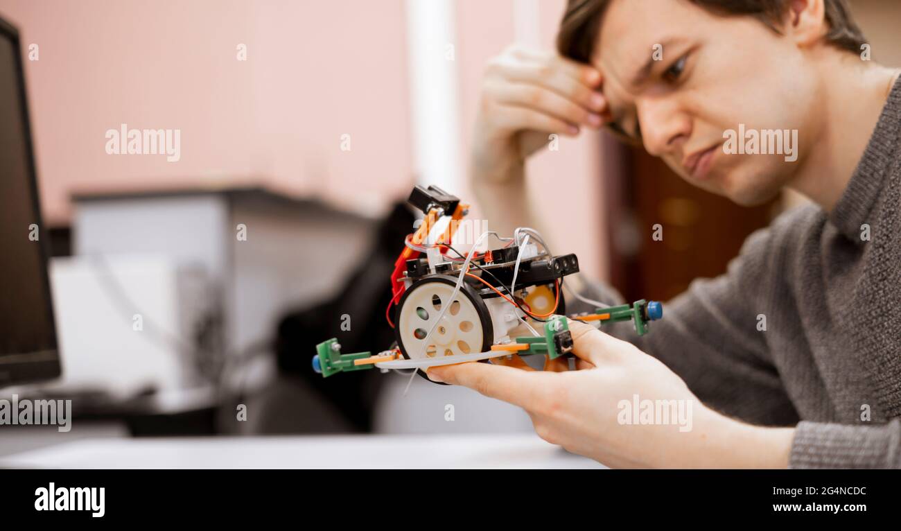 young male constructor scientist assemble the wheeled machine robot in ...