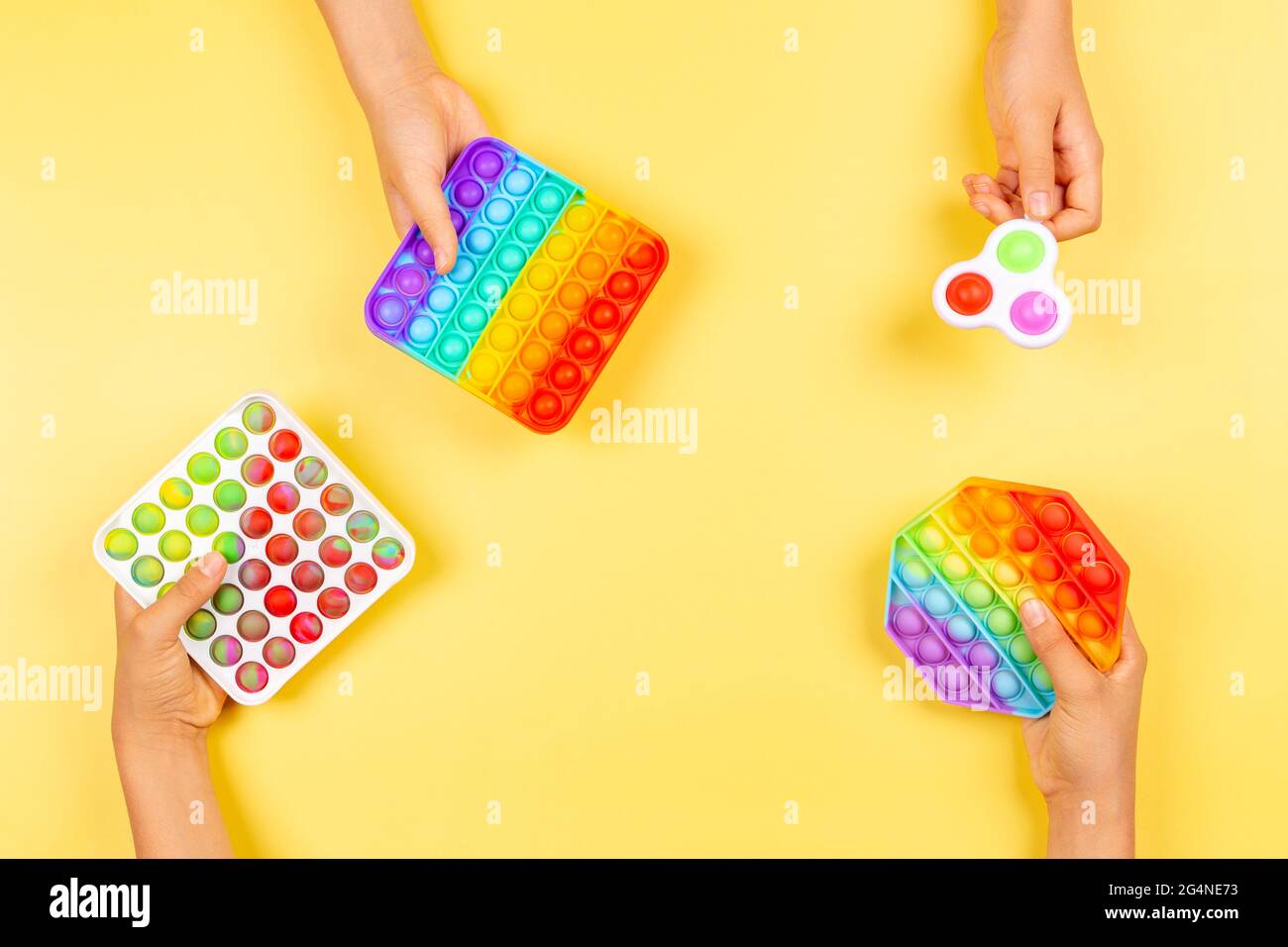 Many hands holding pop it fidget toys on yellow background. Push pop-it ...