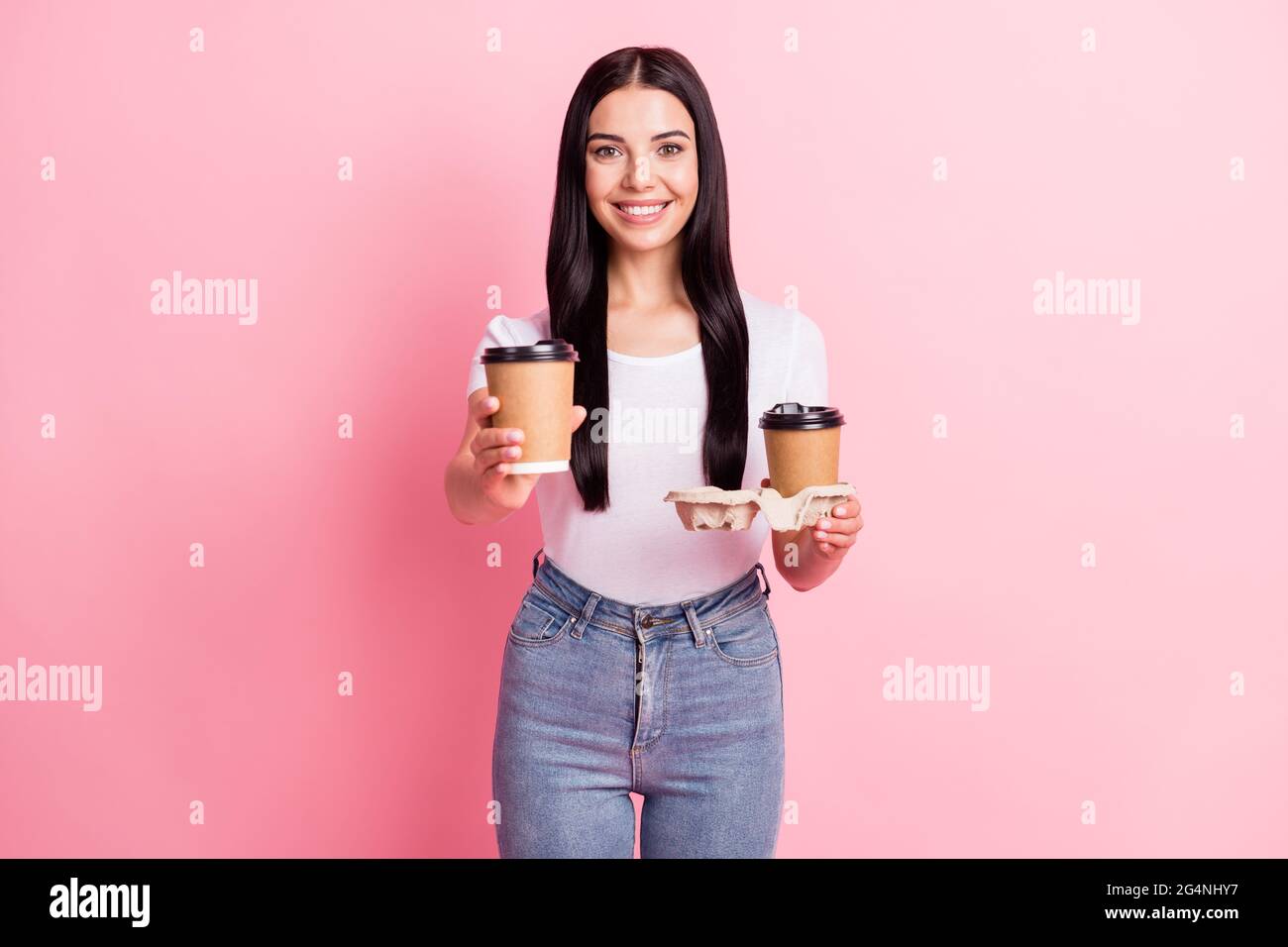 Portrait of attractive cheerful girl bringing carrying two paper cups ...