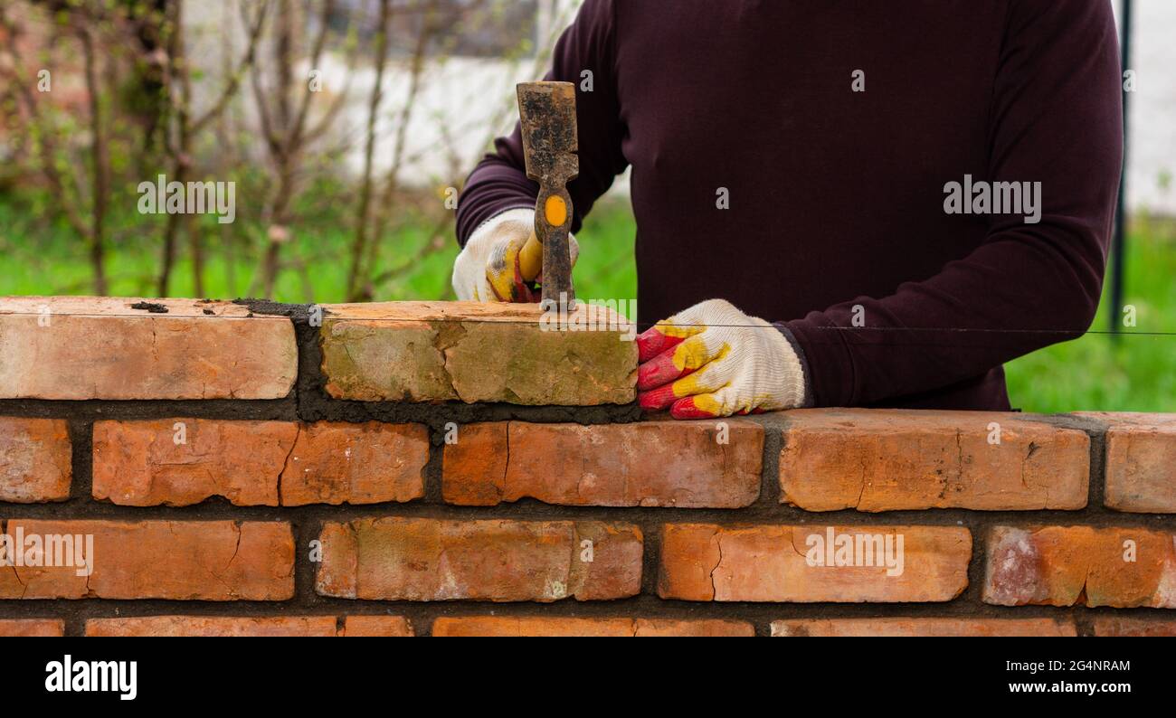 a man builds a brick wall, puts a brick on a cement-sand mortar ...