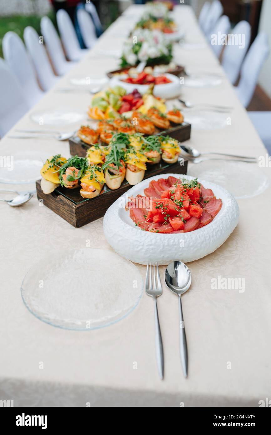 Narrow long dining table outdoors, abundant in the food. Dishes layed ...