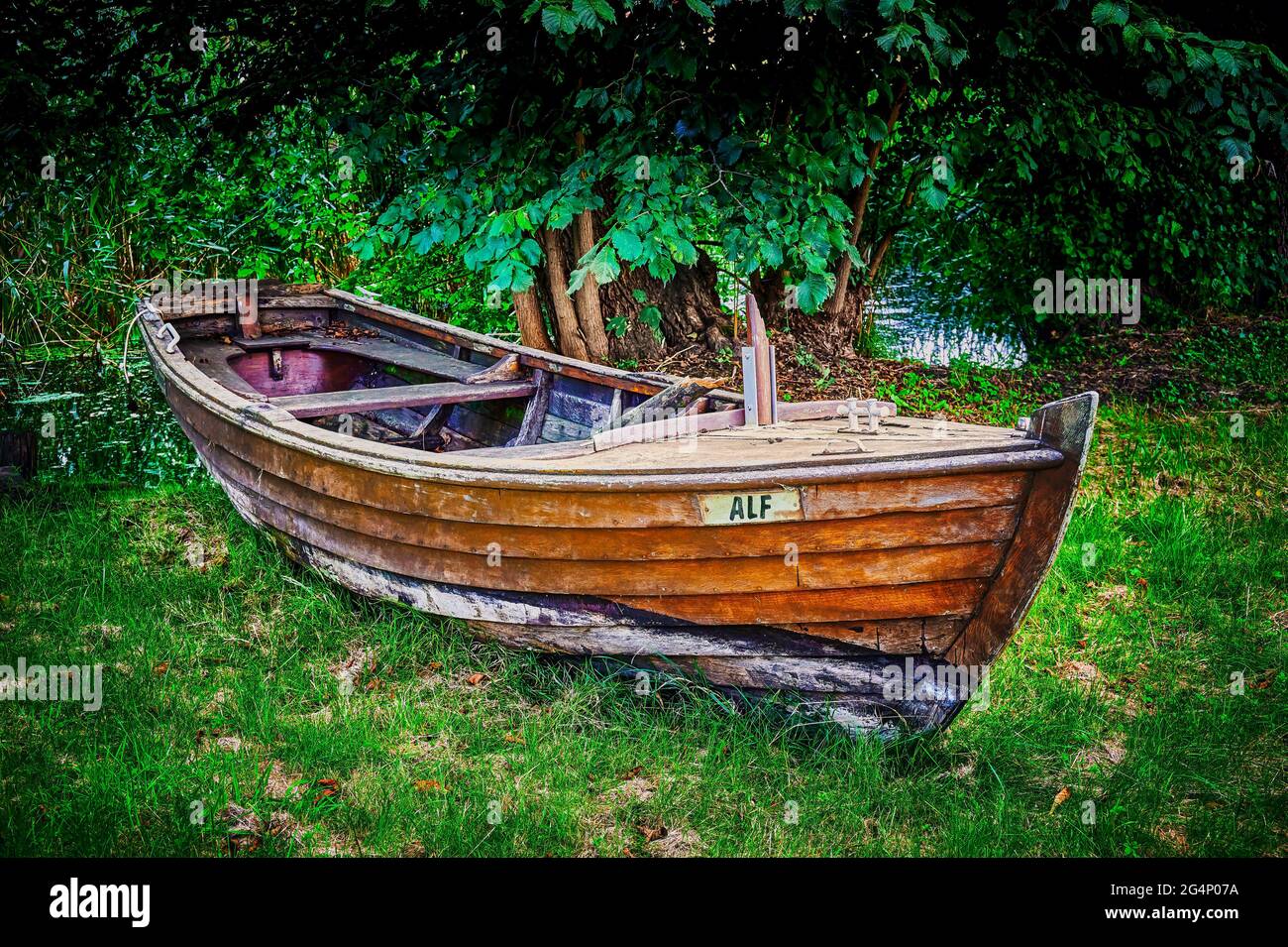 Old wooden rowing boat lying abandoned at the edge of a pond on a ...