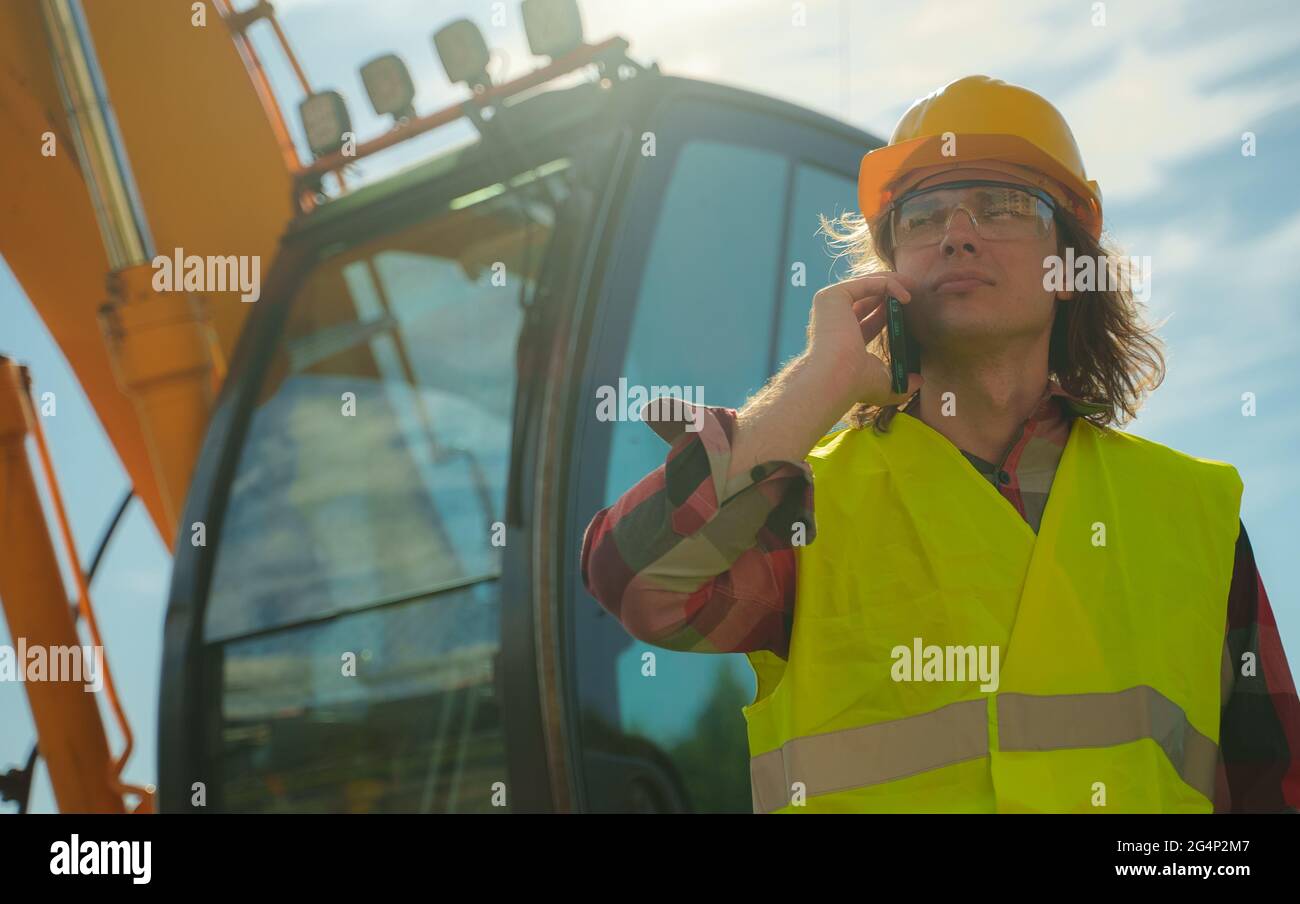 Excavator operator in hard hat talking by smartphone Stock Photo - Alamy