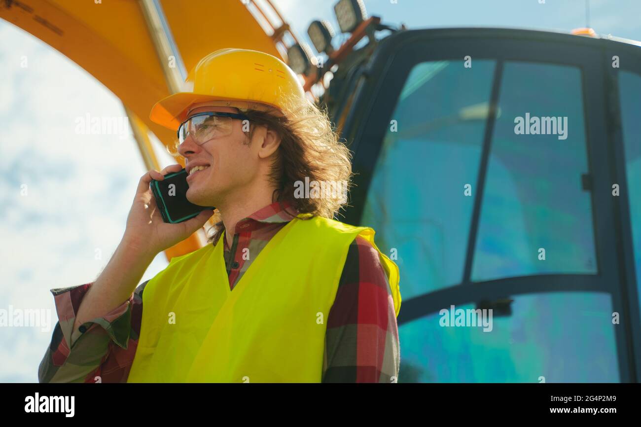 Excavator operator in hard hat talking by smartphone Stock Photo - Alamy