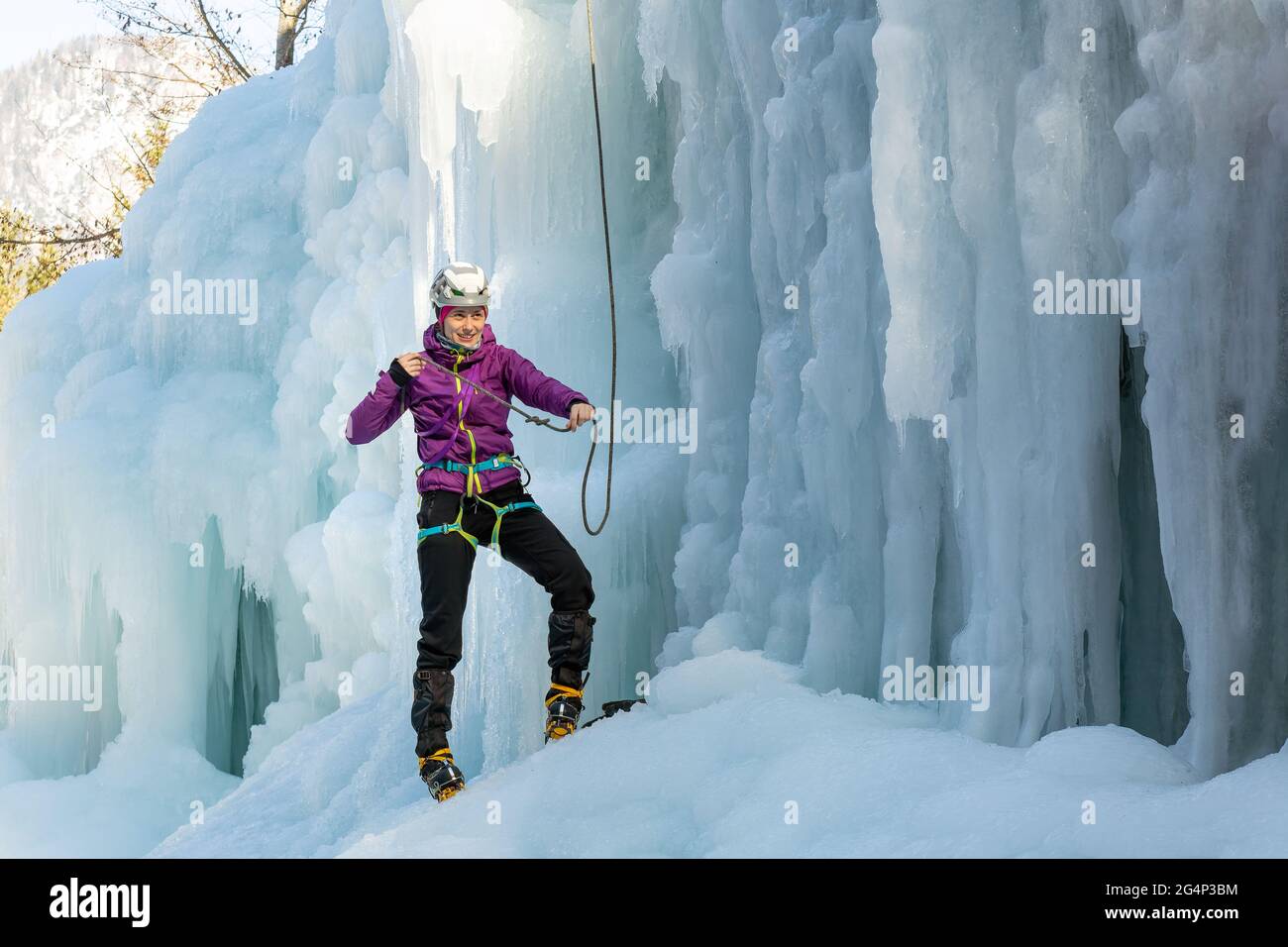 Woman ice climber tying a rope to his harness, preparing for a climb ...