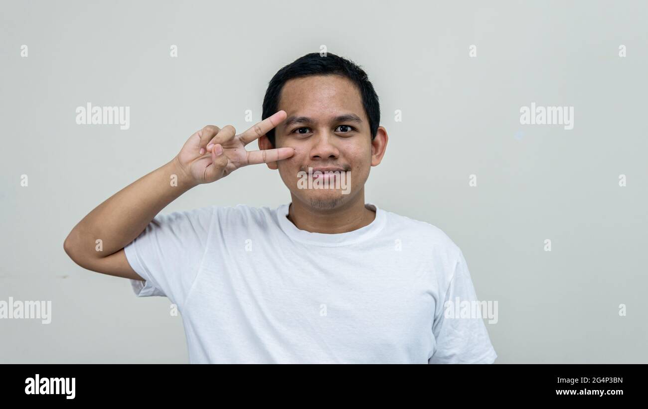 Happy Malay man with a white t-shirt smiling and doing a peace sign ...