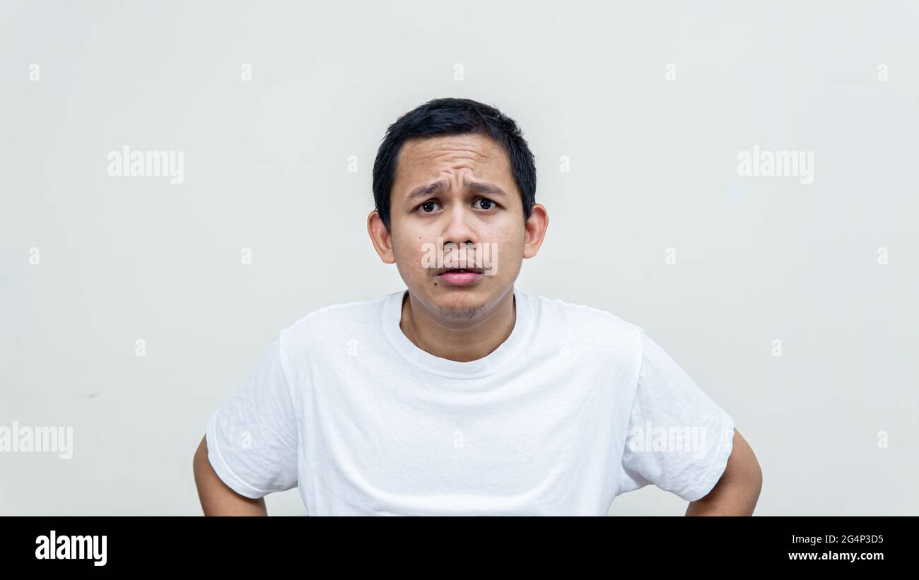 Malay man with a white t-shirt getting angry and mad, frowning his face ...