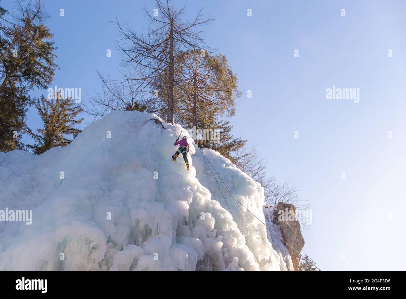 Female ice climber going down an ice waterfall, using a safety top rope ...